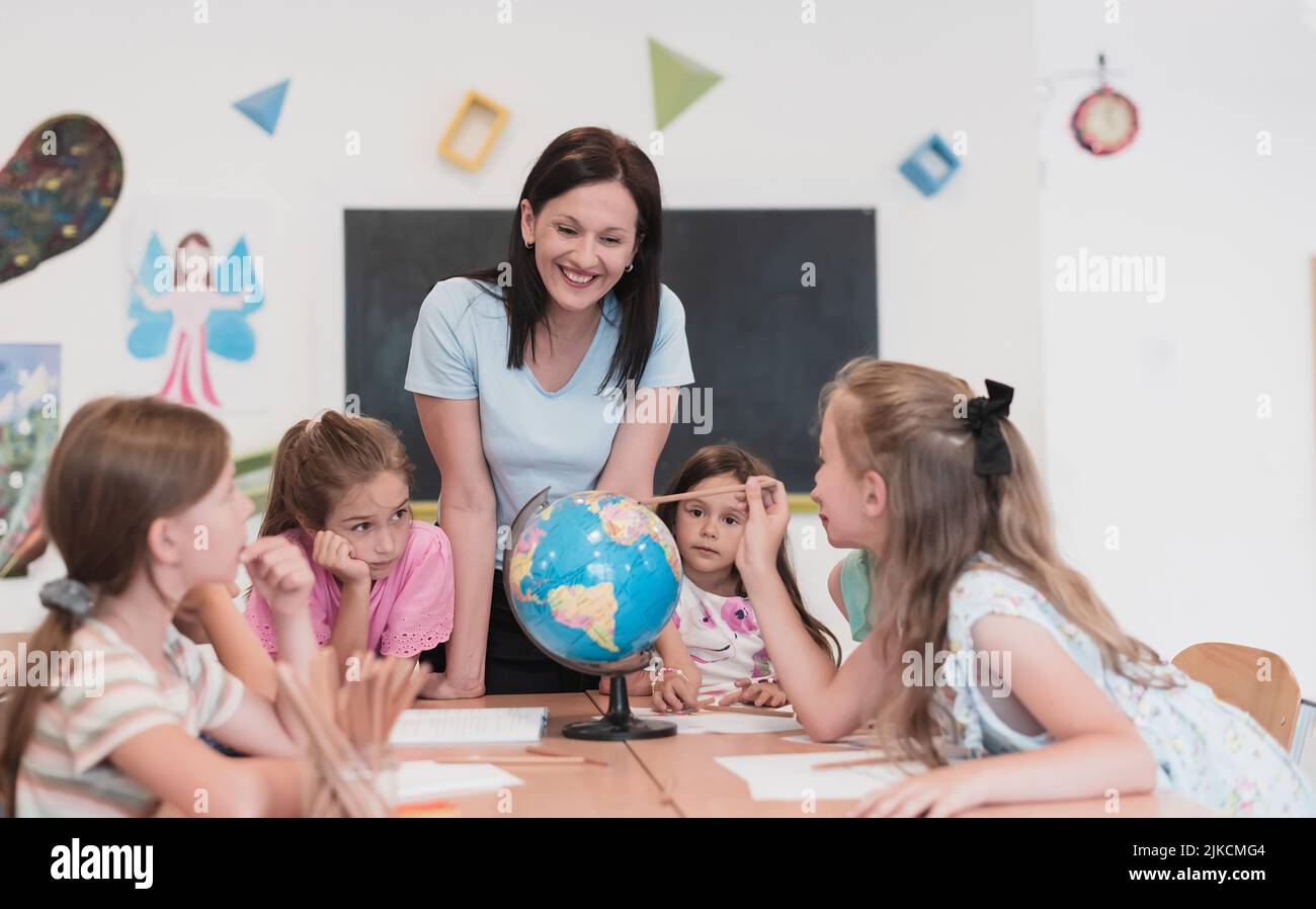 Female teacher with kids in geography class looking at globe. Side view ...