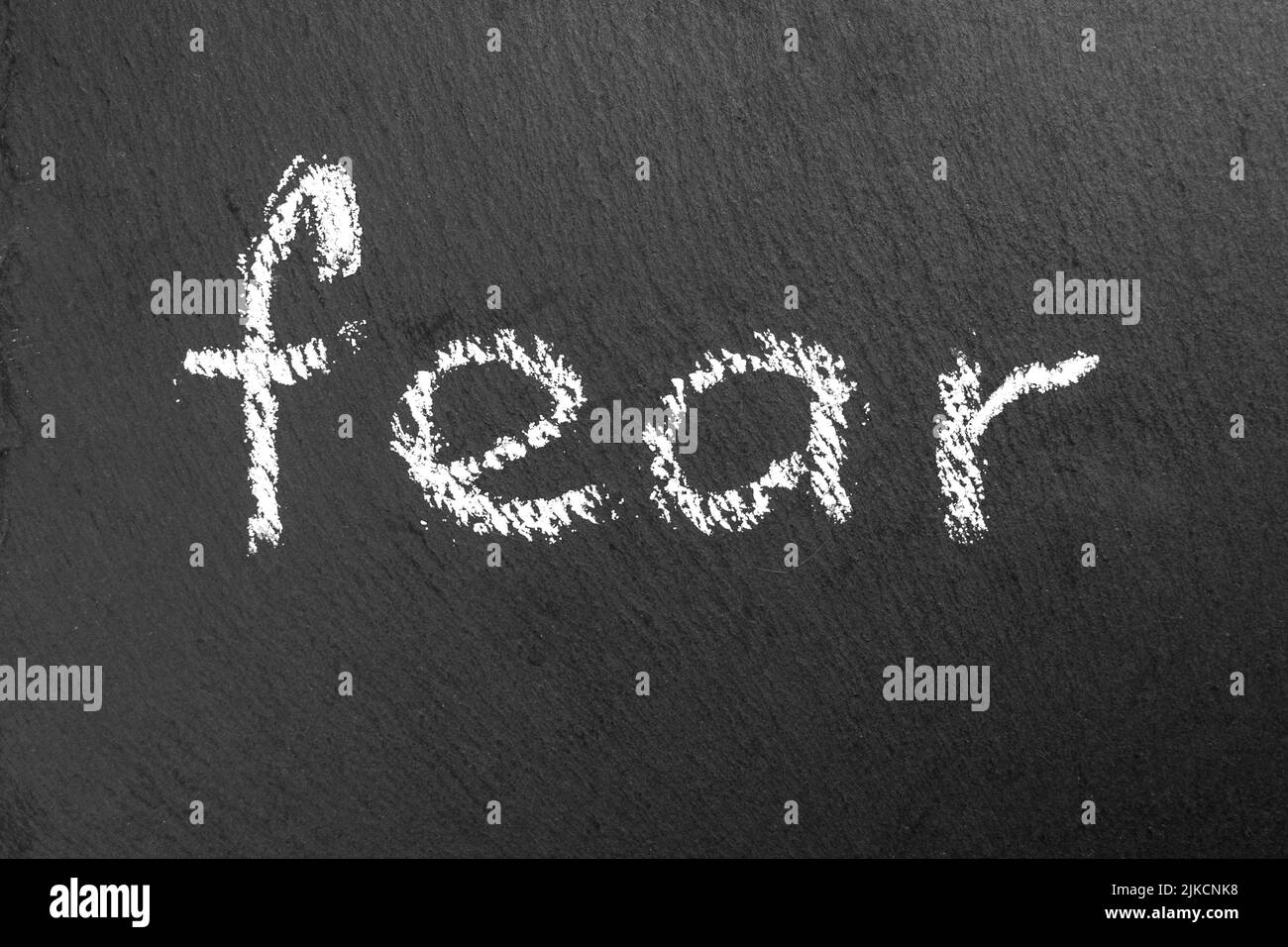 Grunge word FEAR written in chalk on a black rough slate chalkboard ...