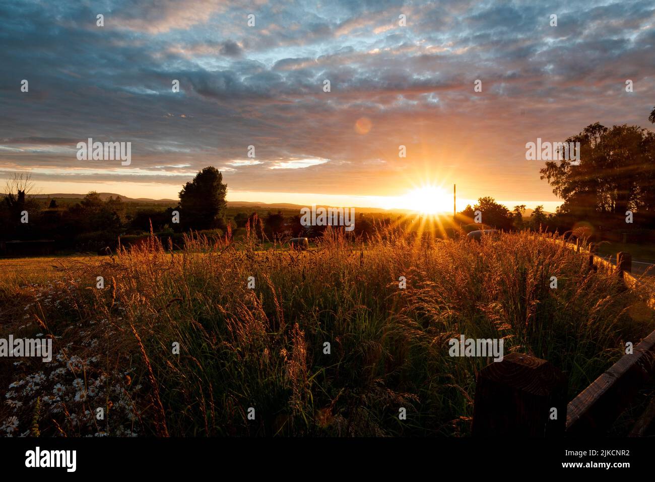A picturesque sunset with cloudy sky on a hill with a fence Stock Photo ...