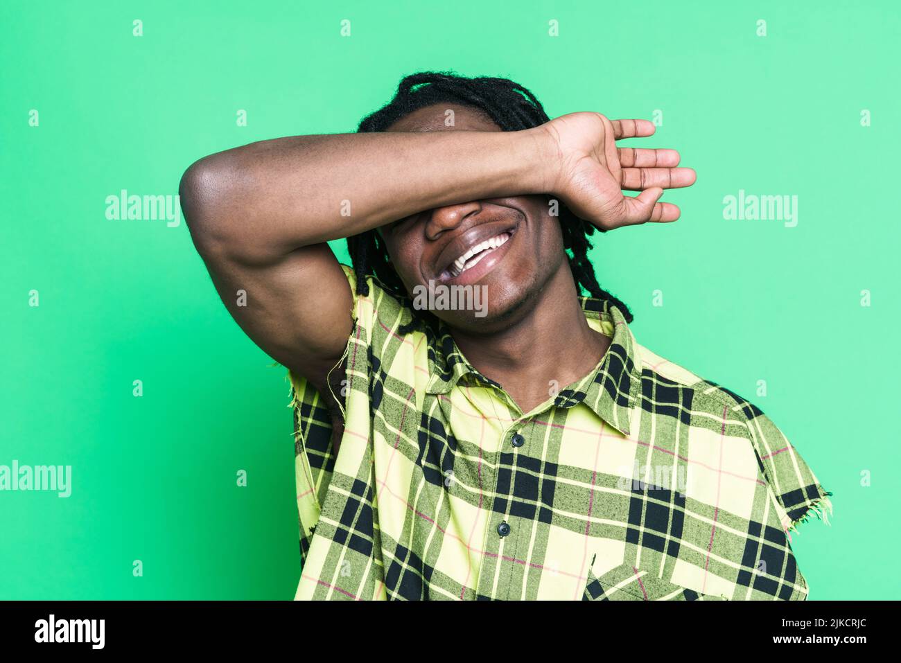 Young black man with dreadlocks laughing while covering his eyes ...