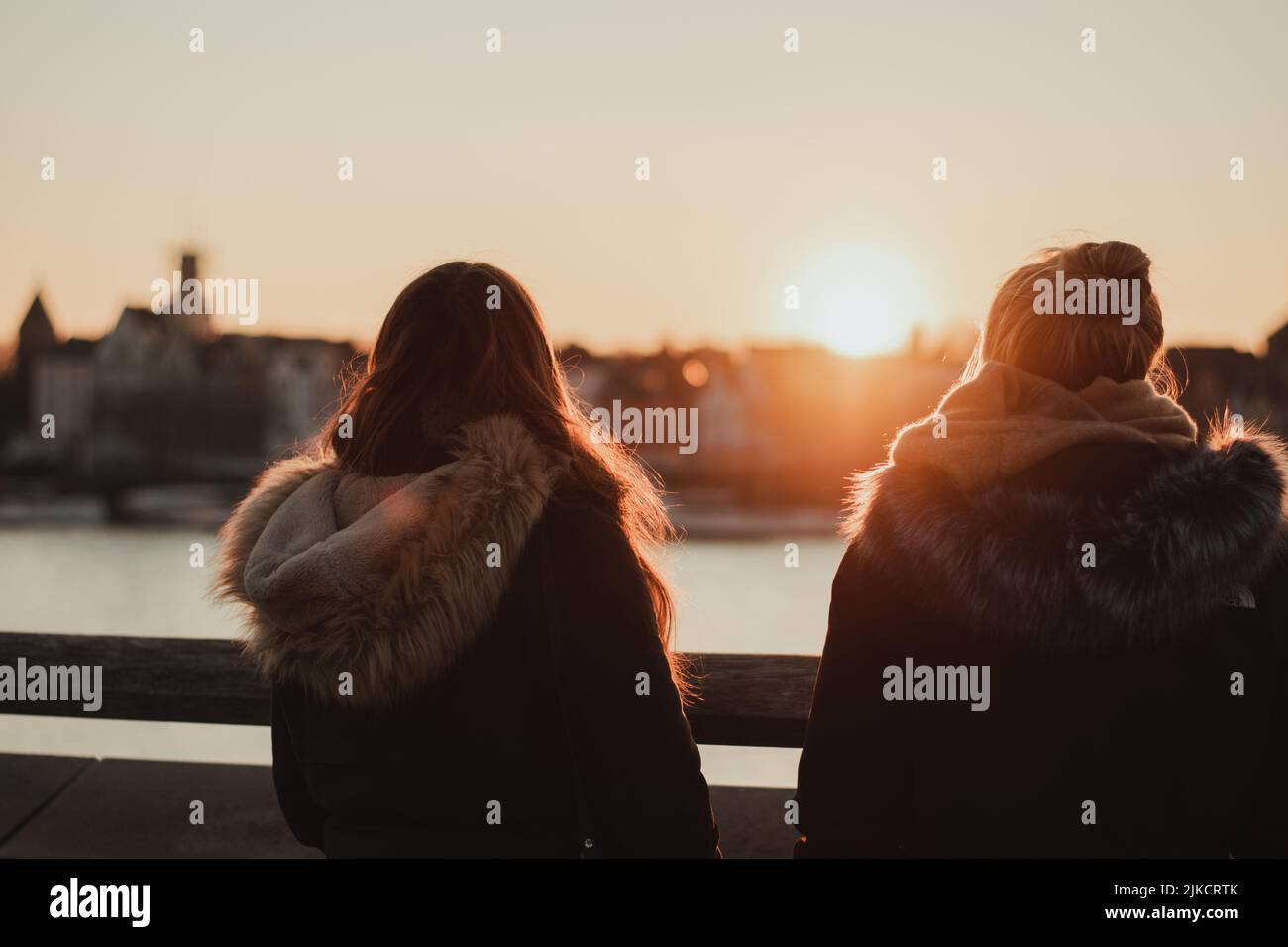 A back view of two female friends looking at the sunset with a warm ...