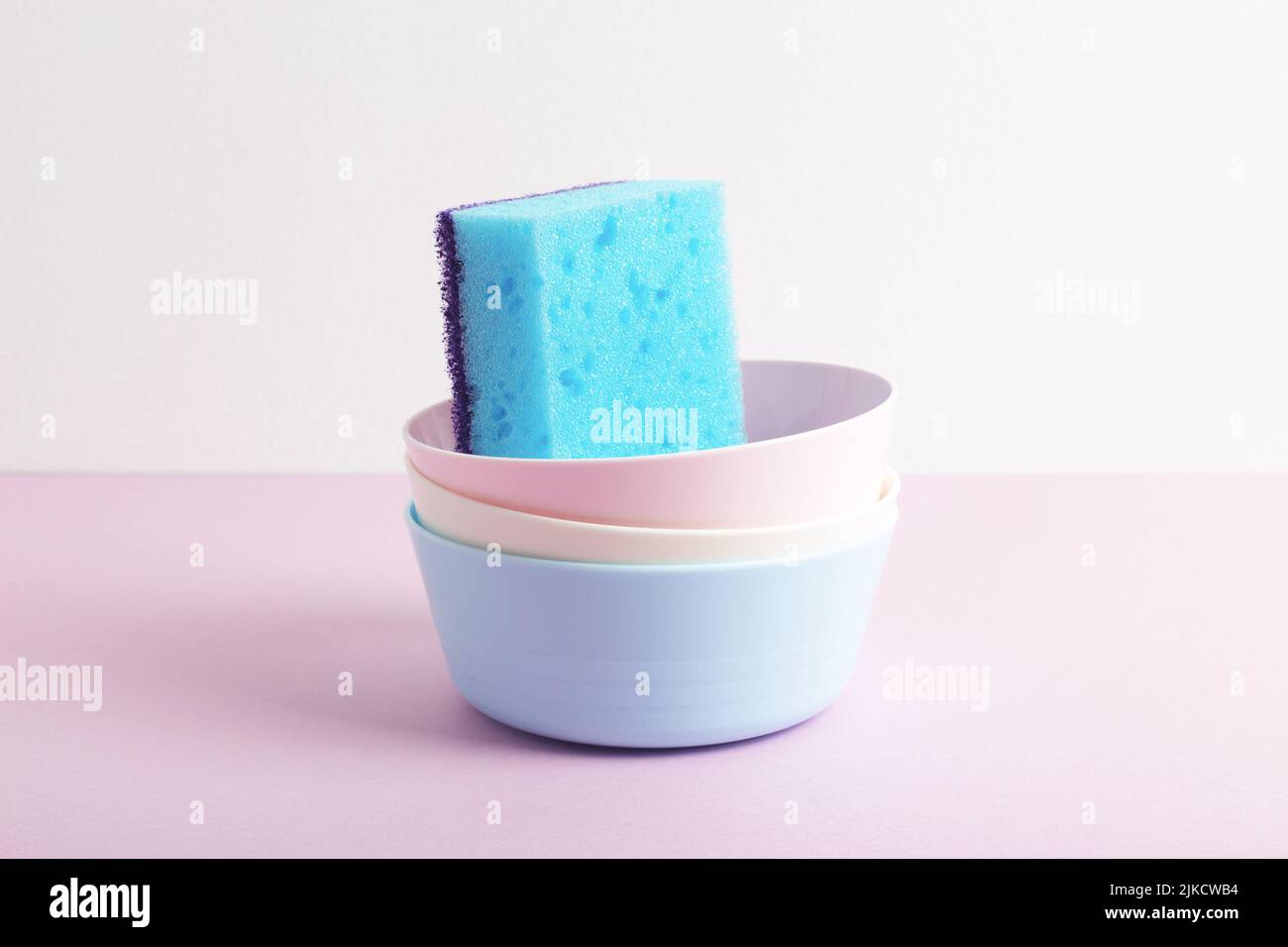 Stack of colourful bowls with blue dishwashing sponge on pink and white ...