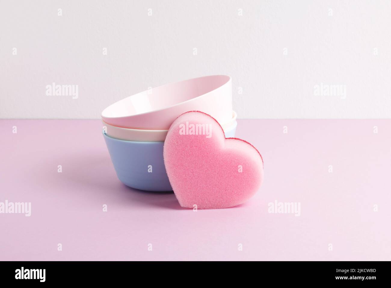 Front view of clean colourful bowls and pink heart shaped sponge ...