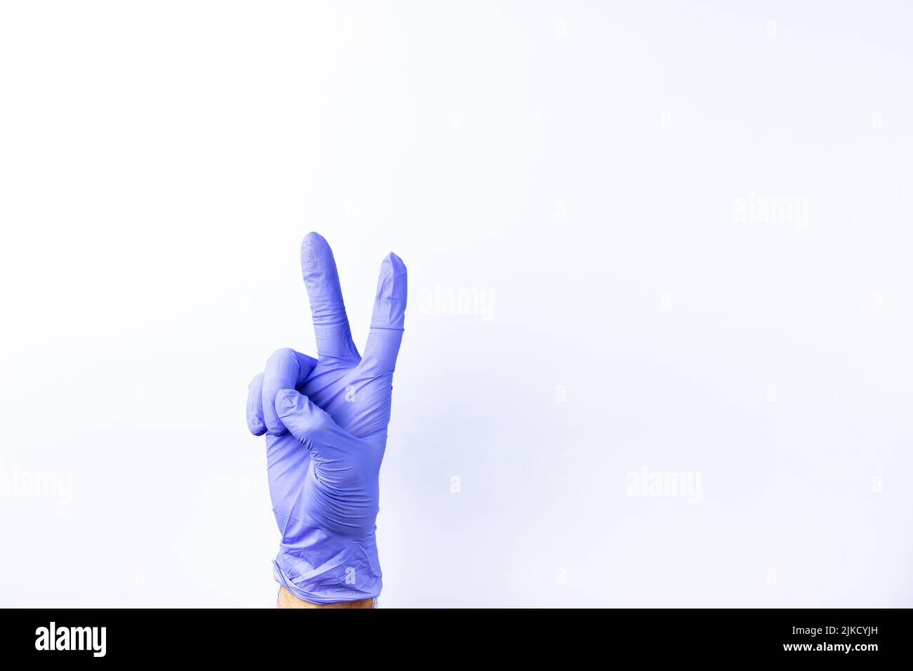 A human hand in a blue medical glove shows a peace sign on a white ...