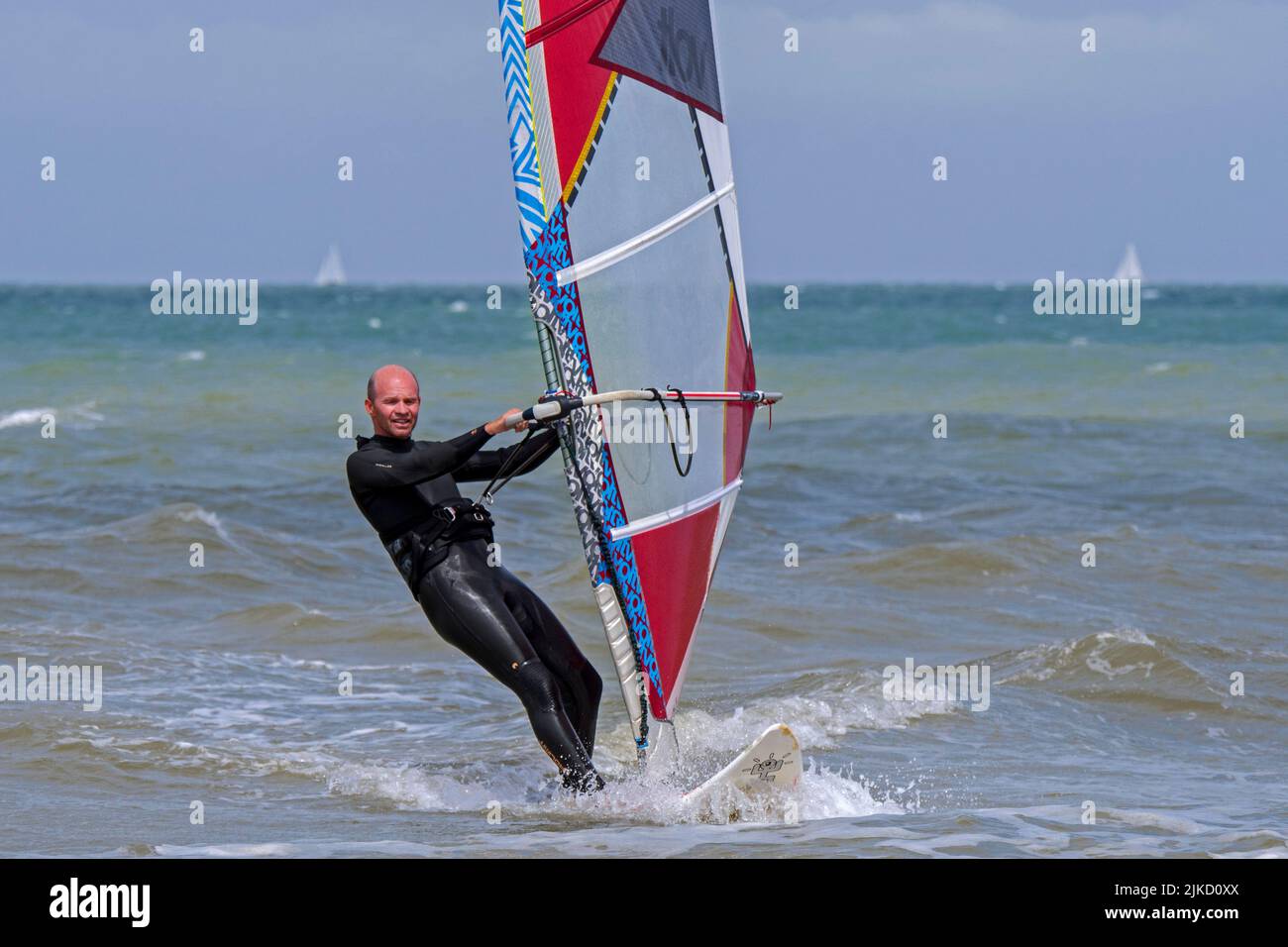 Recreational windsurfer in black wetsuit practising classic windsurfing ...