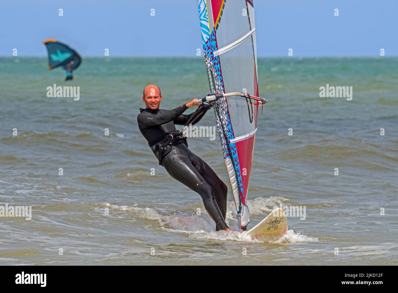 Recreational windsurfer in black wetsuit practising classic windsurfing ...
