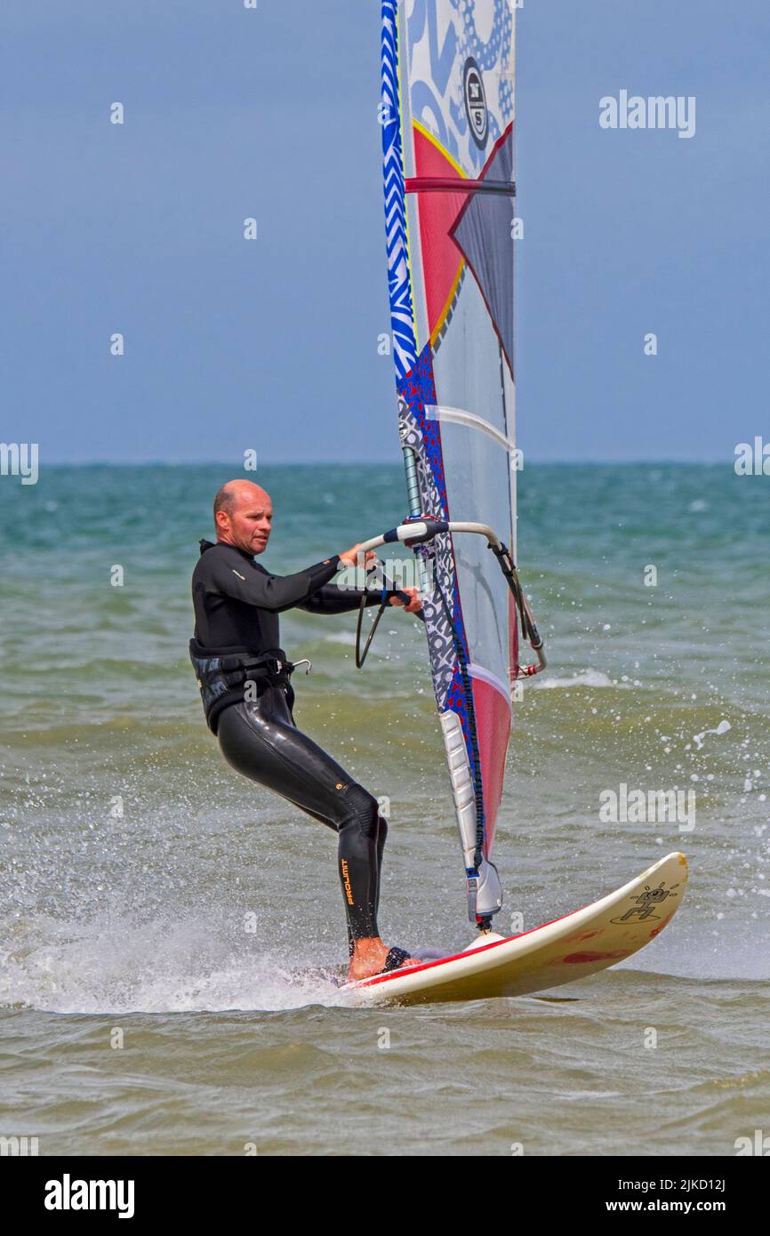 Recreational windsurfer in black wetsuit practising classic windsurfing ...