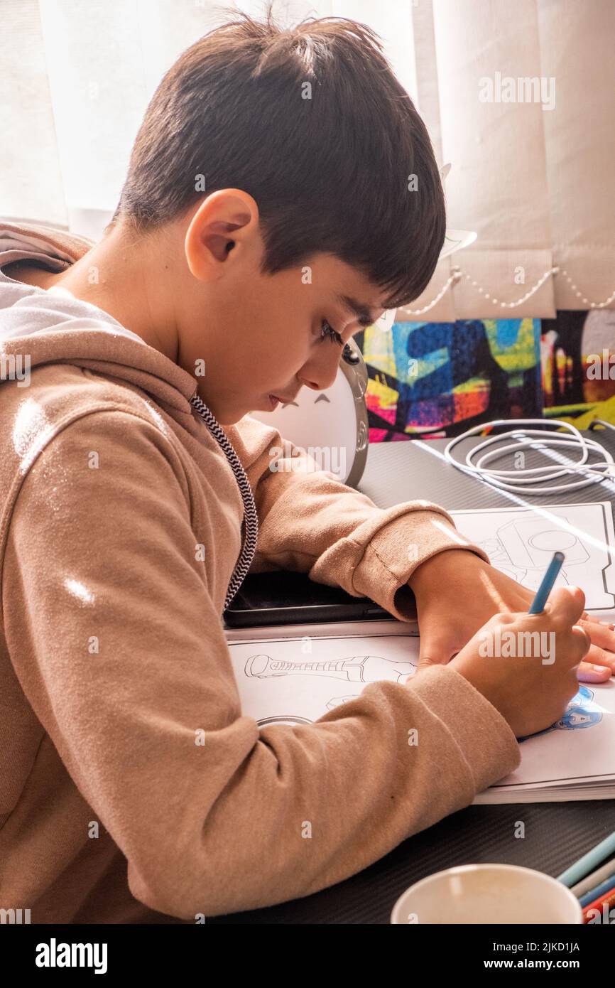 A vertical shot of a boy sitting sideways and coloring drawings Stock ...