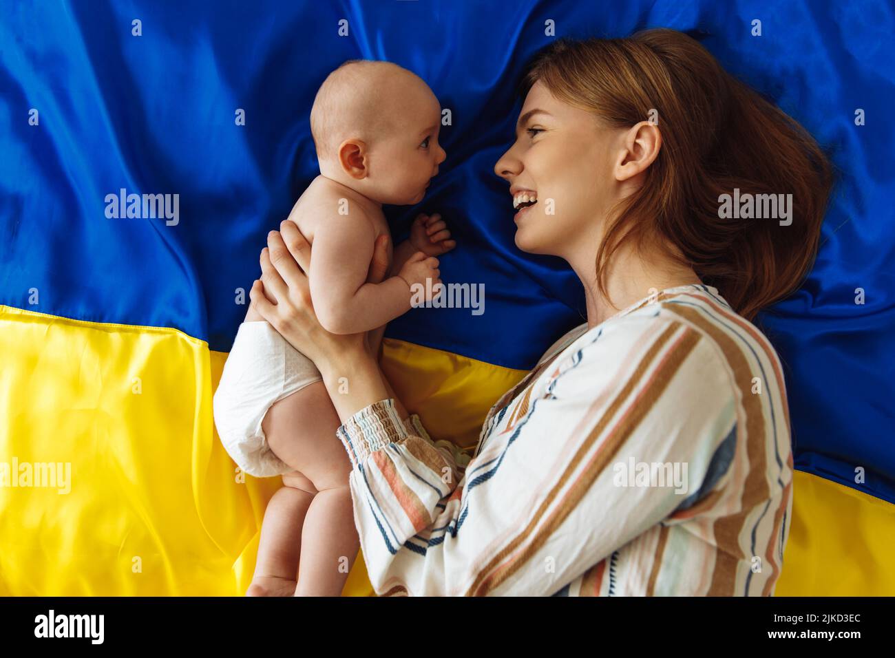 Loving caring mother with her newborn baby lies on the background of the Ukrainian Blue and ...