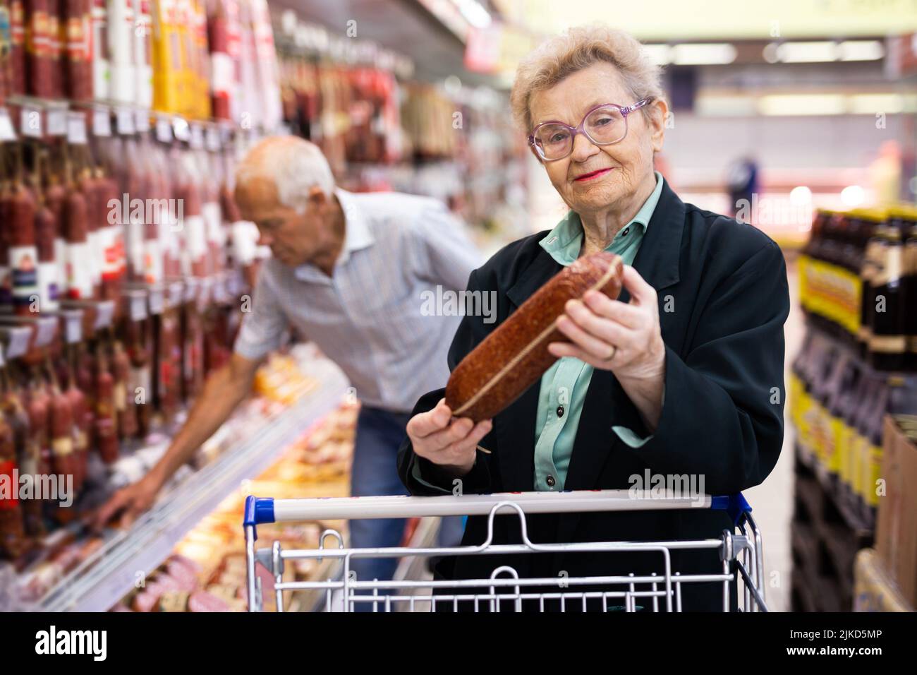 mature woman with glasses picks out salami in the meat section of the ...