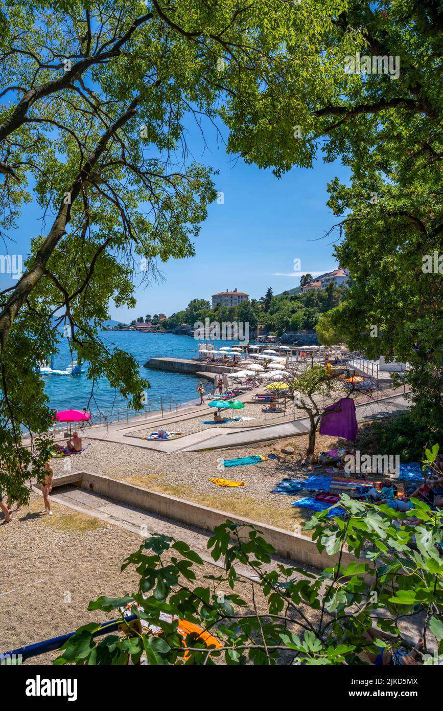 Holiday makers on tree lined pebble beach and Adriatic Sea at Lovran ...