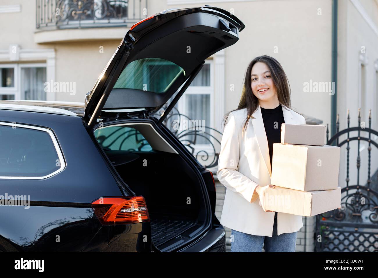 Young business woman picking up parcels from a car trunk, coming home ...