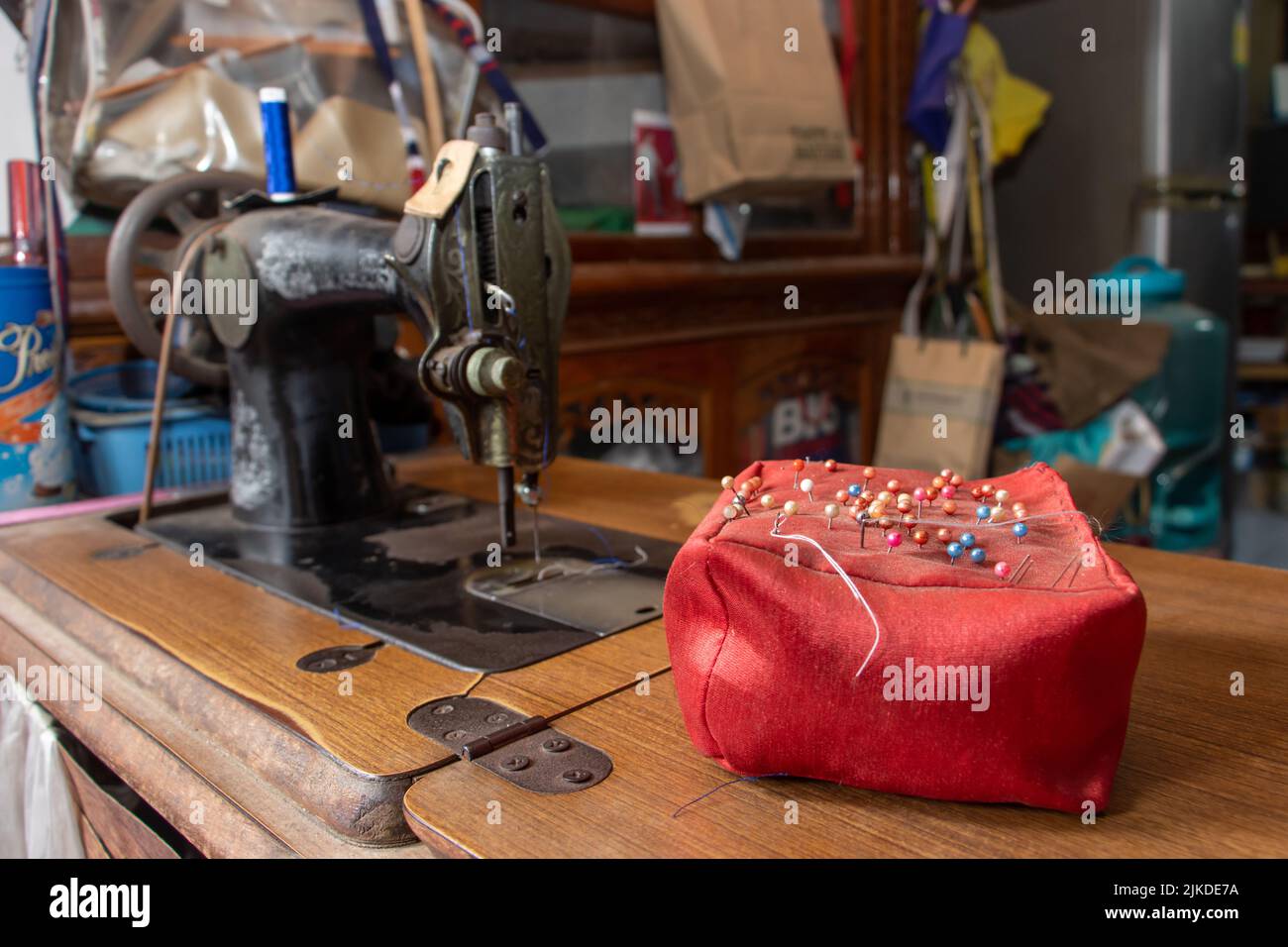 A pincushion is lying on a table with an old foot-drive sewing machine ...