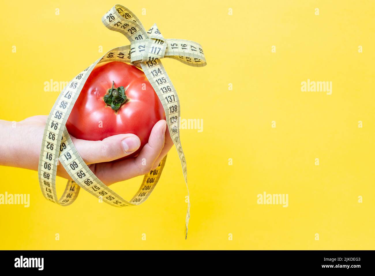 Girl's hand holding a tomato tied with tape measure and bow, on yellow ...