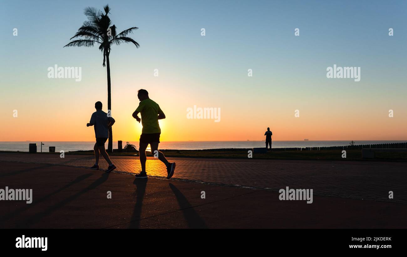 Athlete runners silhouetted training beach promenade at sunrise over ...