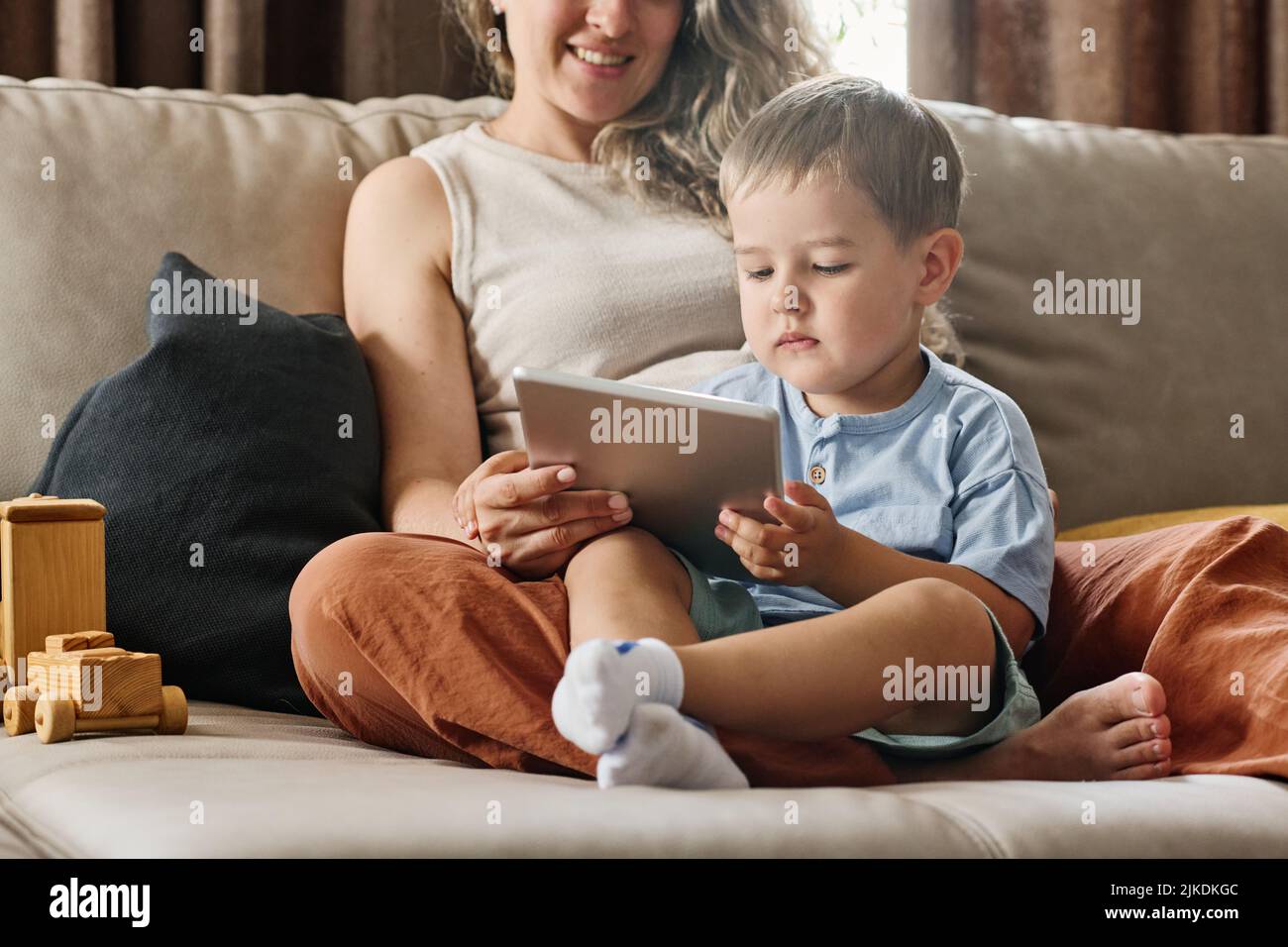 Serious toddler in casualwear looking at screen of tablet held by his ...