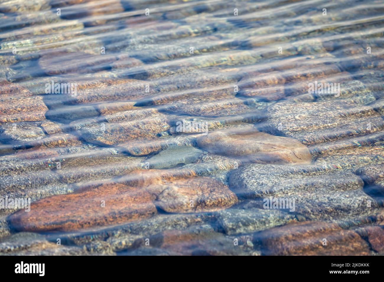Colourful pebbles seen through crystal clear glacier melt water lake ...