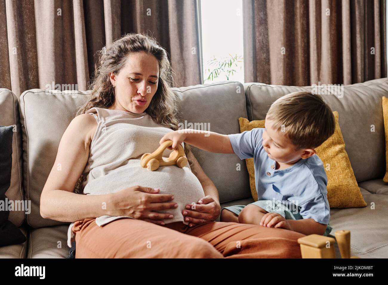 Cute toddler moving wooden toy car over belly of his pregnant mother ...