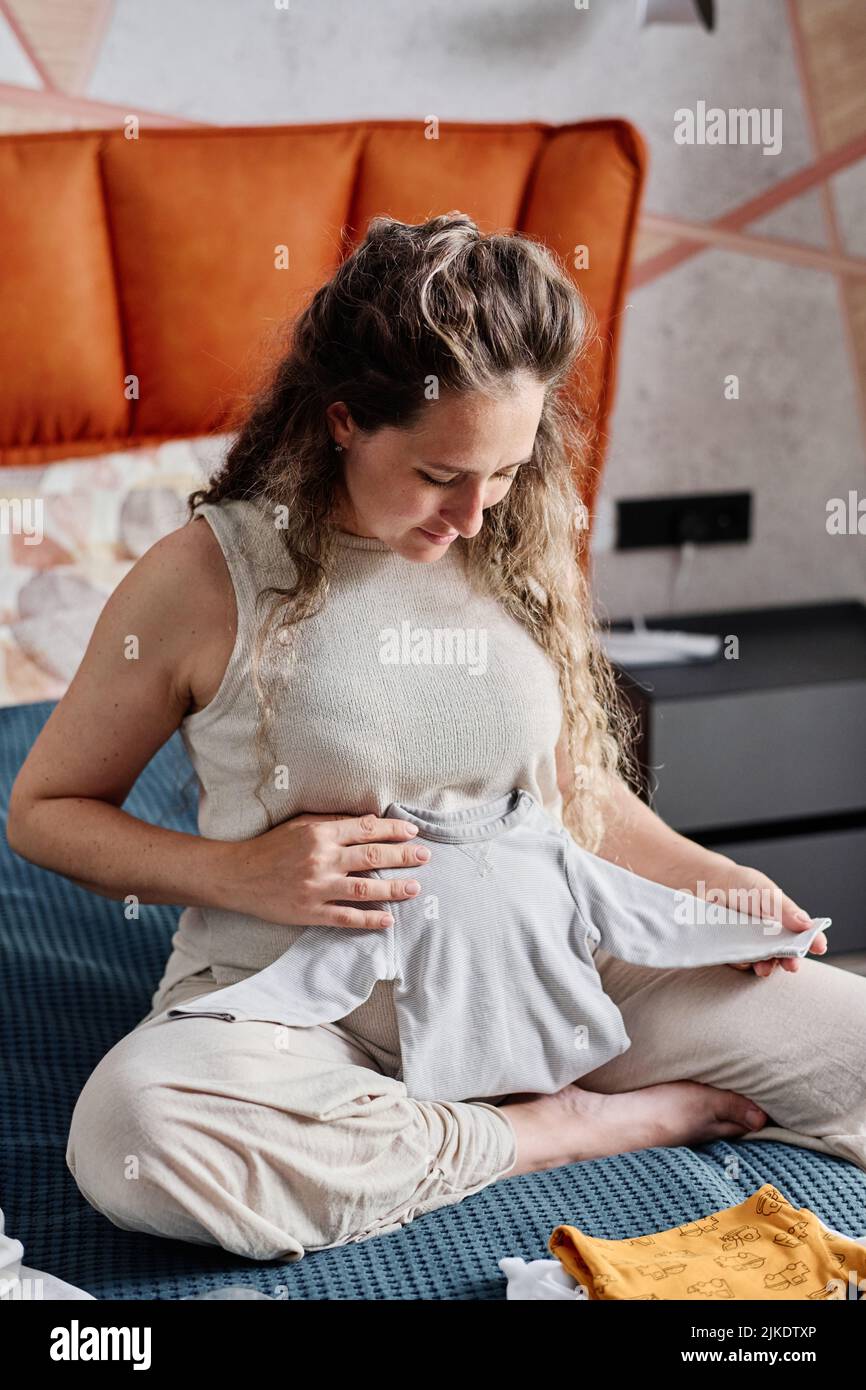 Pregnant woman sitting bed looking baby clothes hi-res stock ...