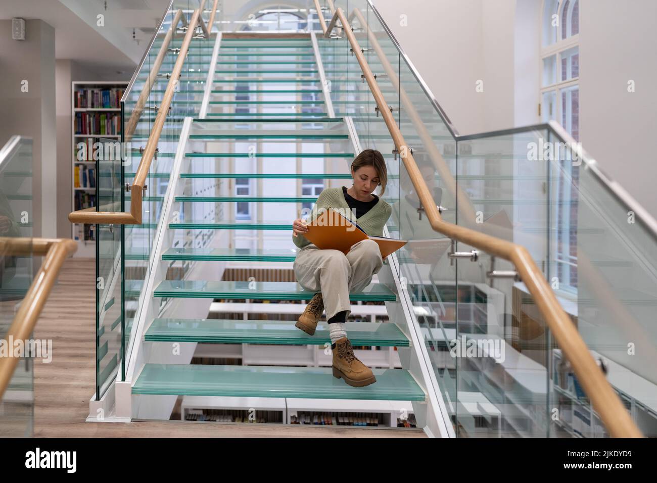 Curious female reader sits on modern glass stairs step reading favorite ...