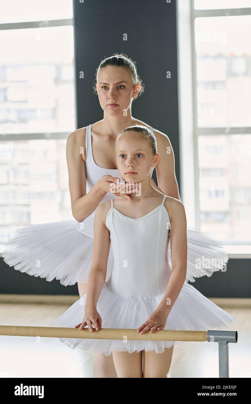 Young ballet teacher and her youthful learner in white tutu standing by ...
