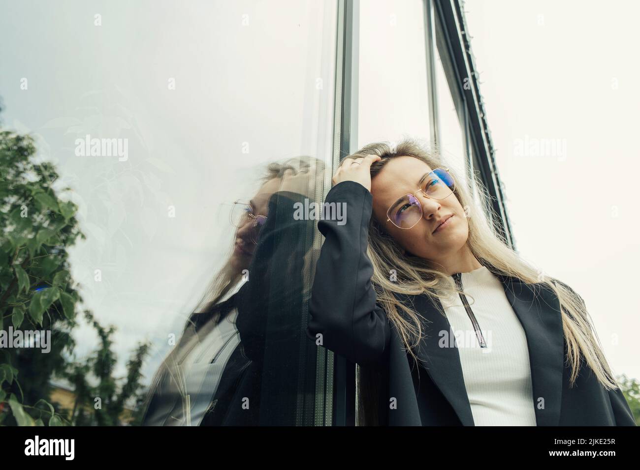 A beautiful woman stands leaning against the window of a building ...