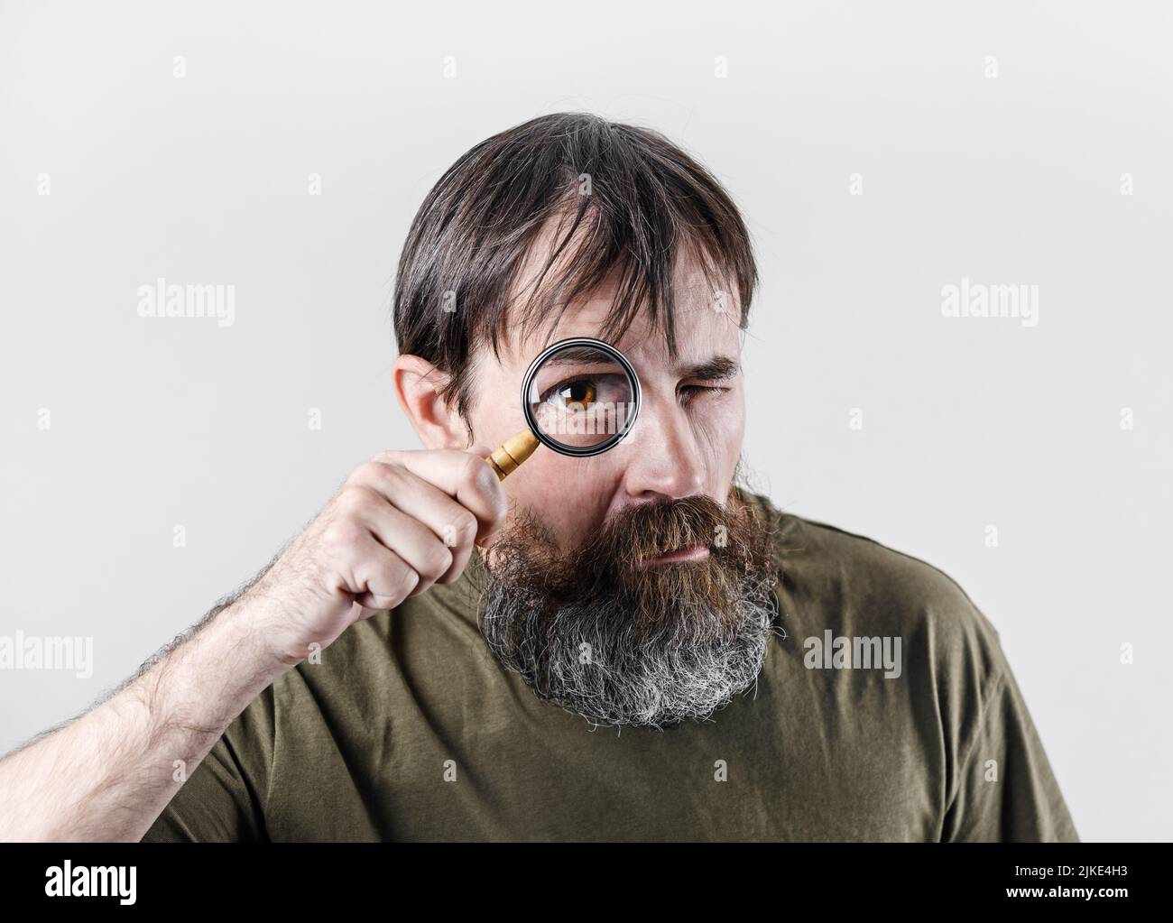 Bearded man looking through magnifying glass. Surprised Male detective ...