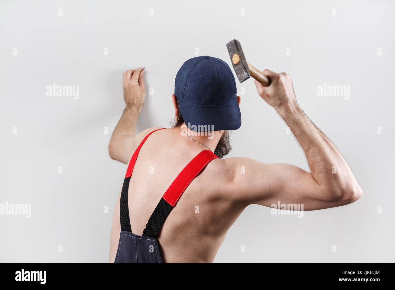 Muscular worker hammers a nail with a hammer. Man with a hammer. Back ...