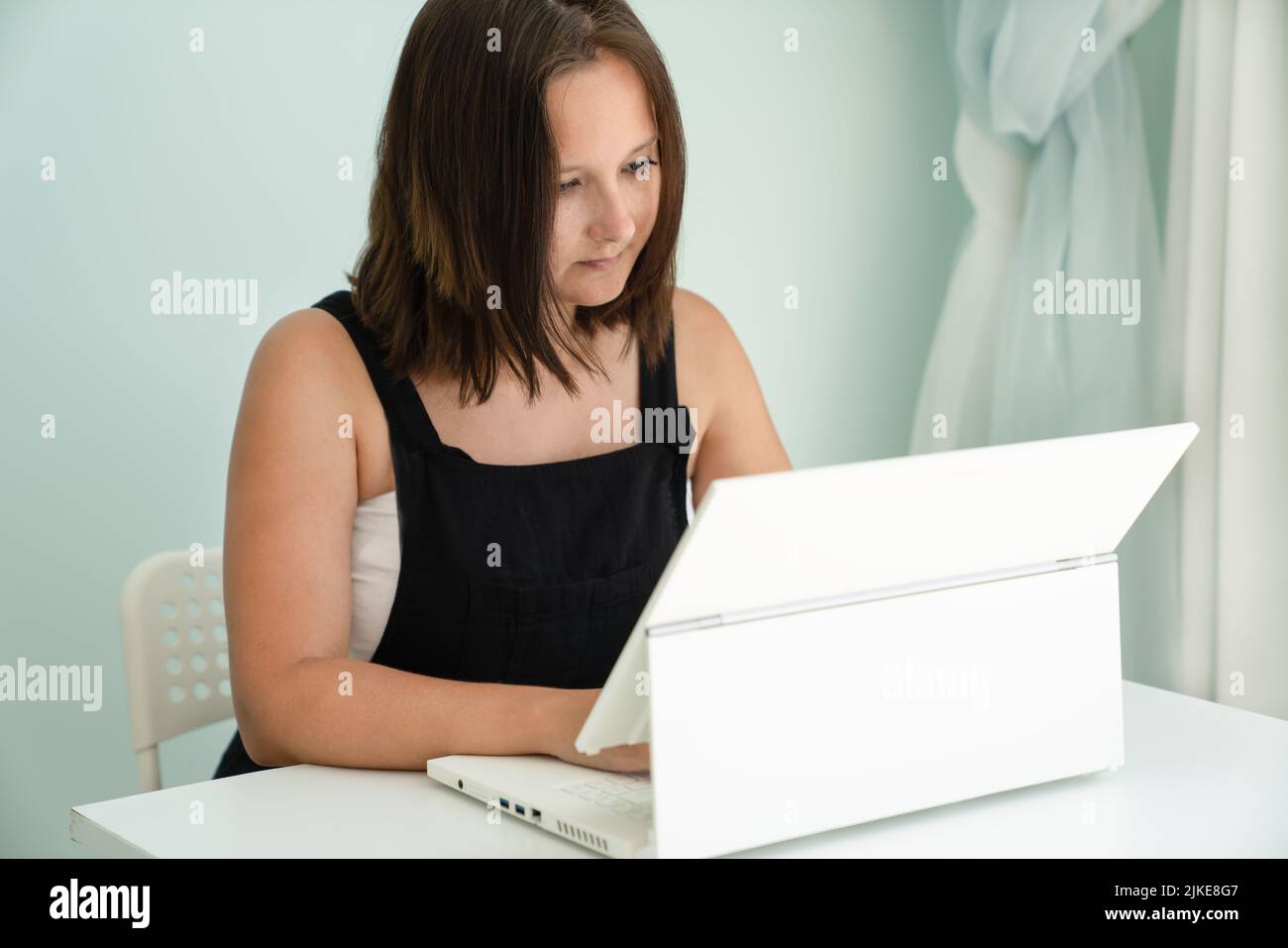 Girl is sitting in front of her white laptop transformer at desk in her ...