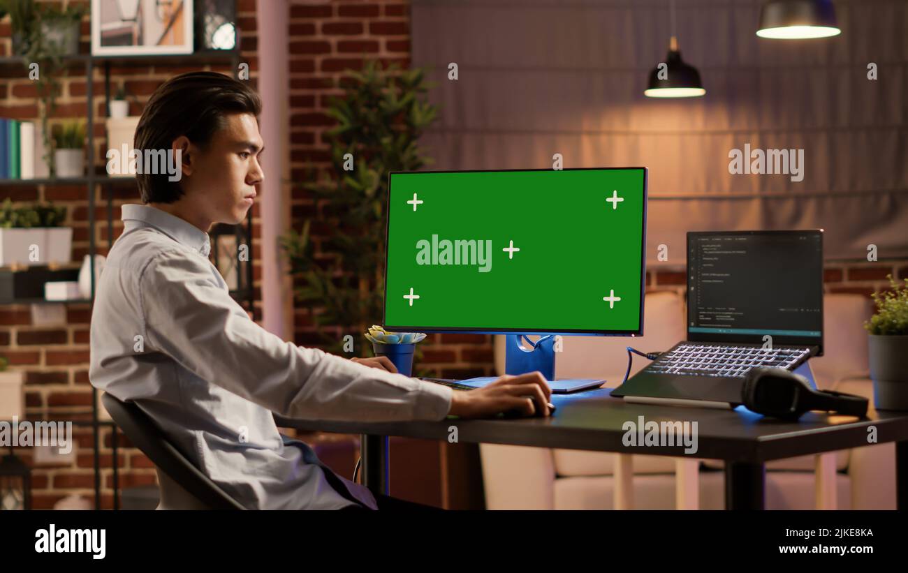 Asian businessman looking at computer with greenscreen on display, analyzing isolated copyspace ...