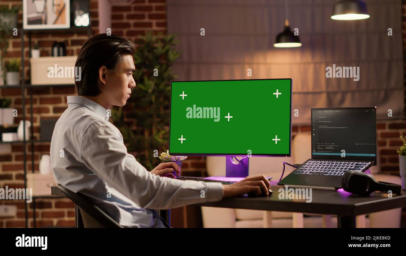 Asian businessman working on computer with greenscreen in living room. Looking at blank ...