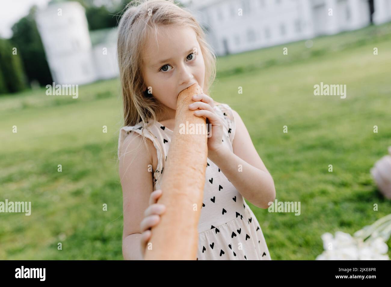 A little girl is holding a big loaf of bread. Funny happy child bites ...