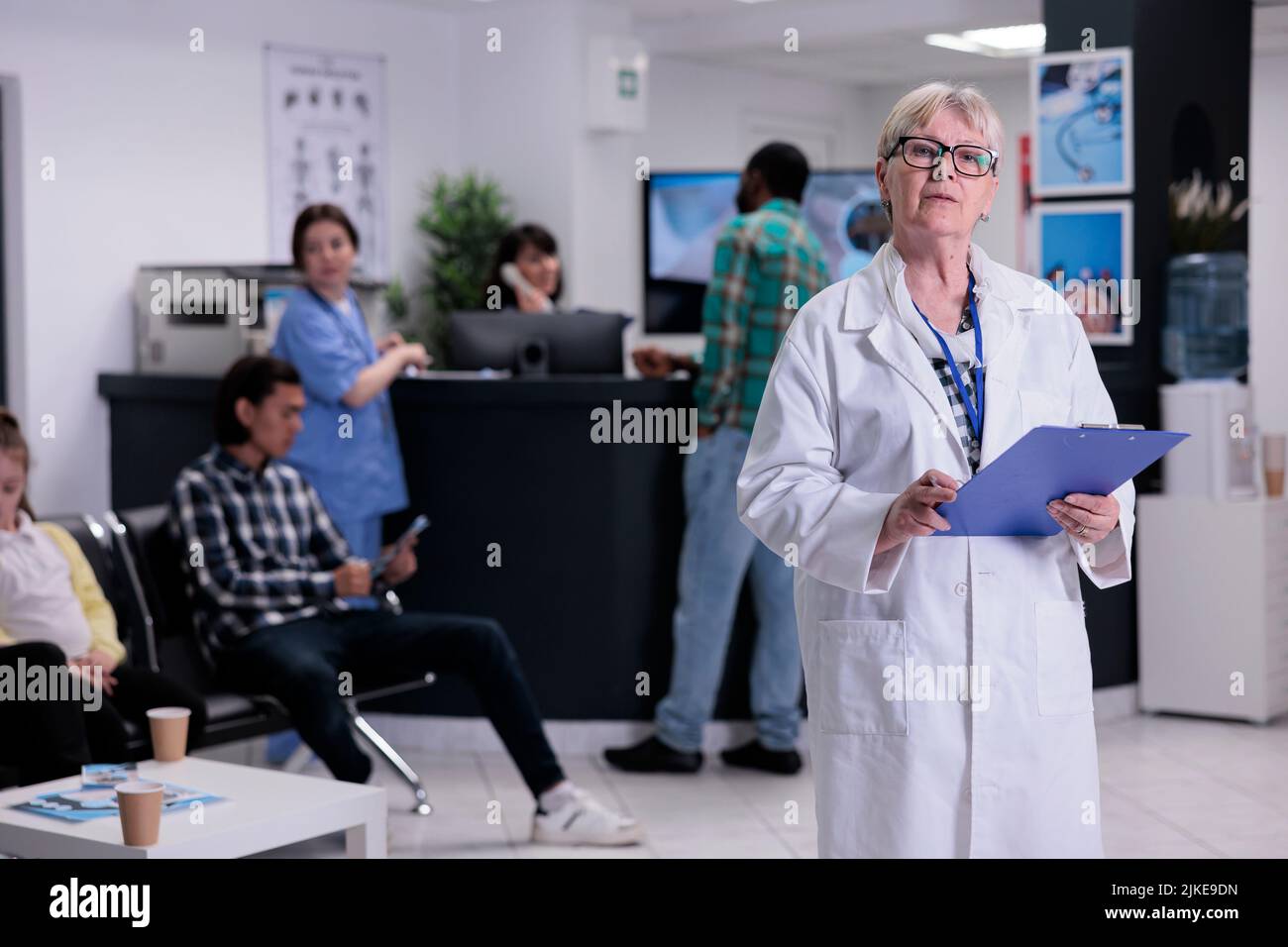 Portrait of confident senior medic with stethoscope standing in busy ...
