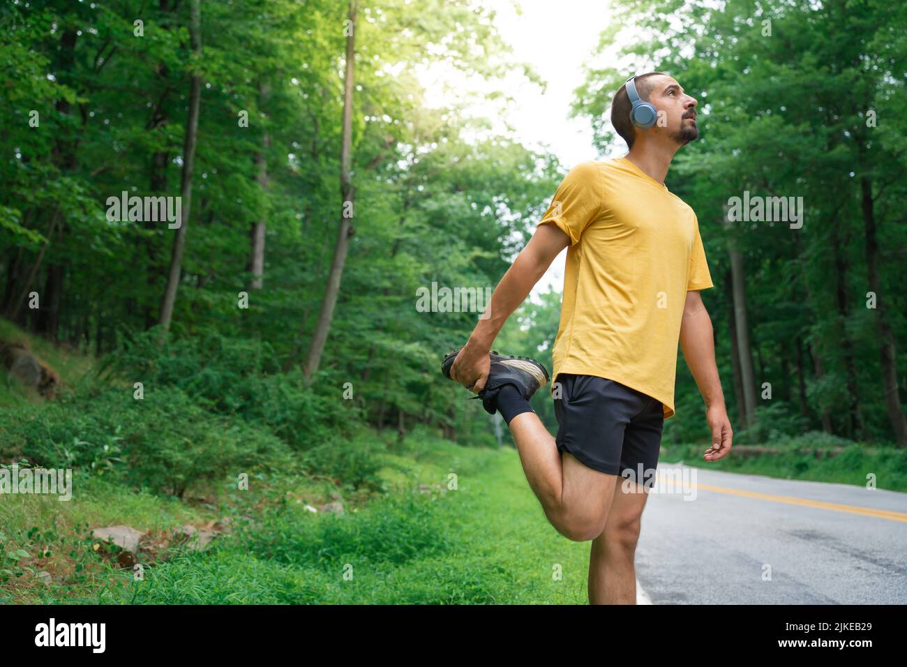 Young fitness man runner stretching legs before run in road in nature ...