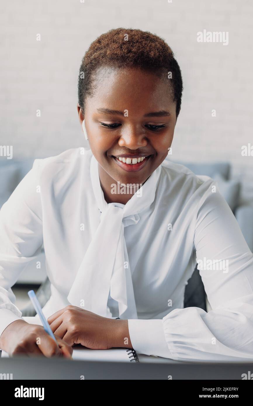 Afro woman student using laptop, taking notes, watching webinar in ...