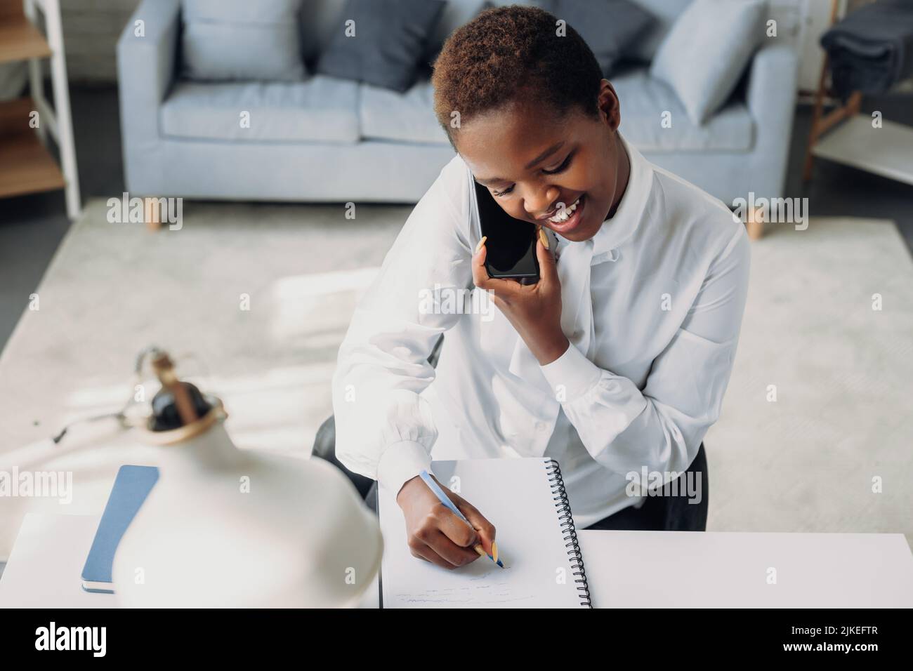 Afro businesswoman having phone conversation taking notes at work ...