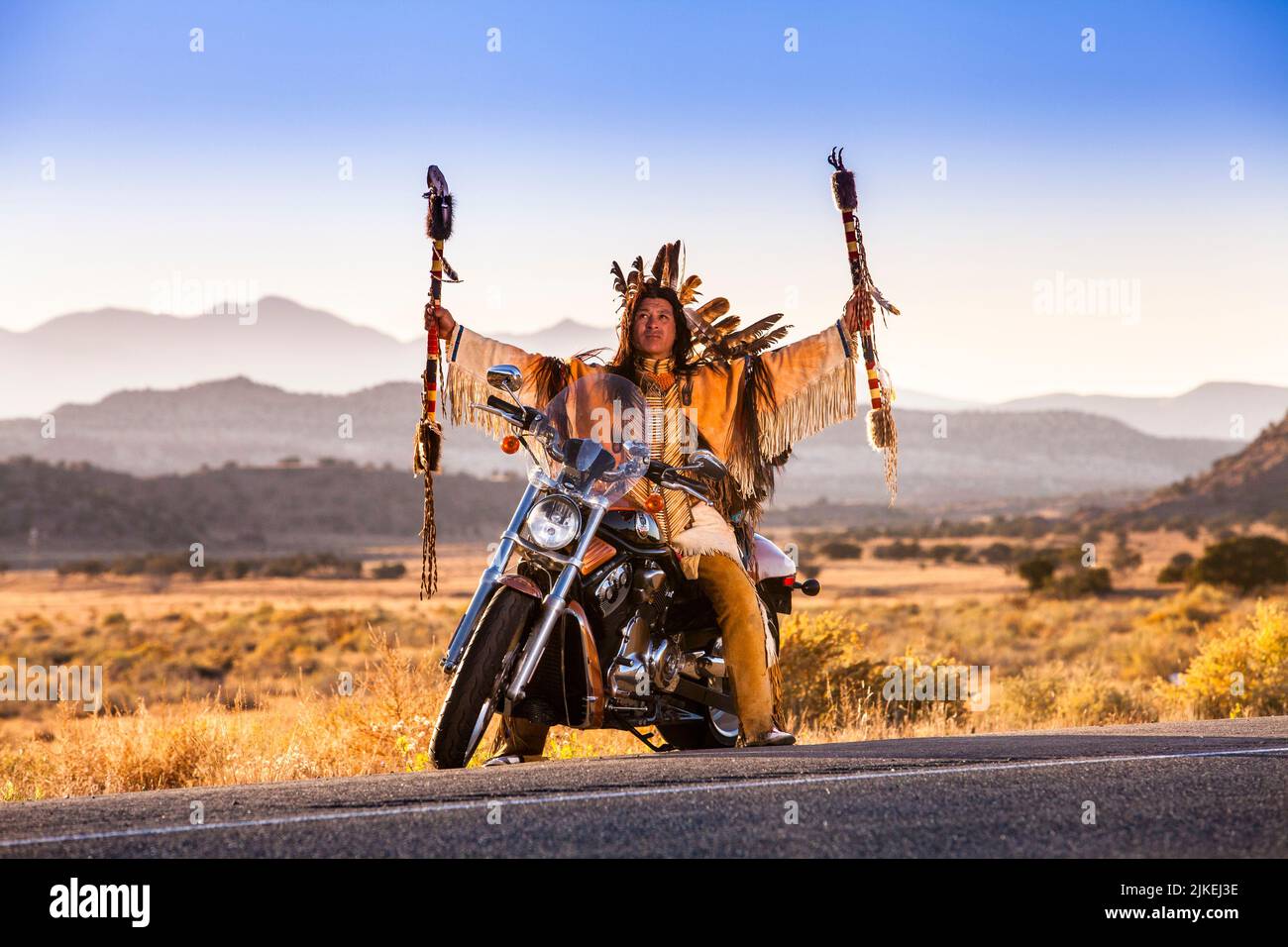 Traditionally dressed Native American man holds up two coup sticks ...