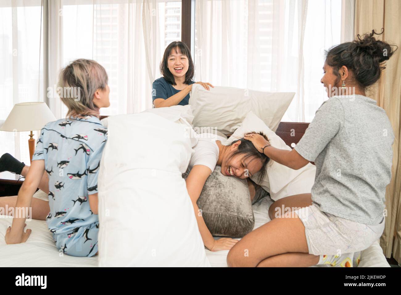 Multi-ethnic girls pillow fighting in bedroom, sleep over party concept ...
