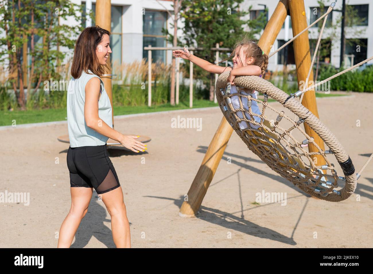 Mom and daughter swing on a round swing. Caucasian woman and little girl have fun on the ...