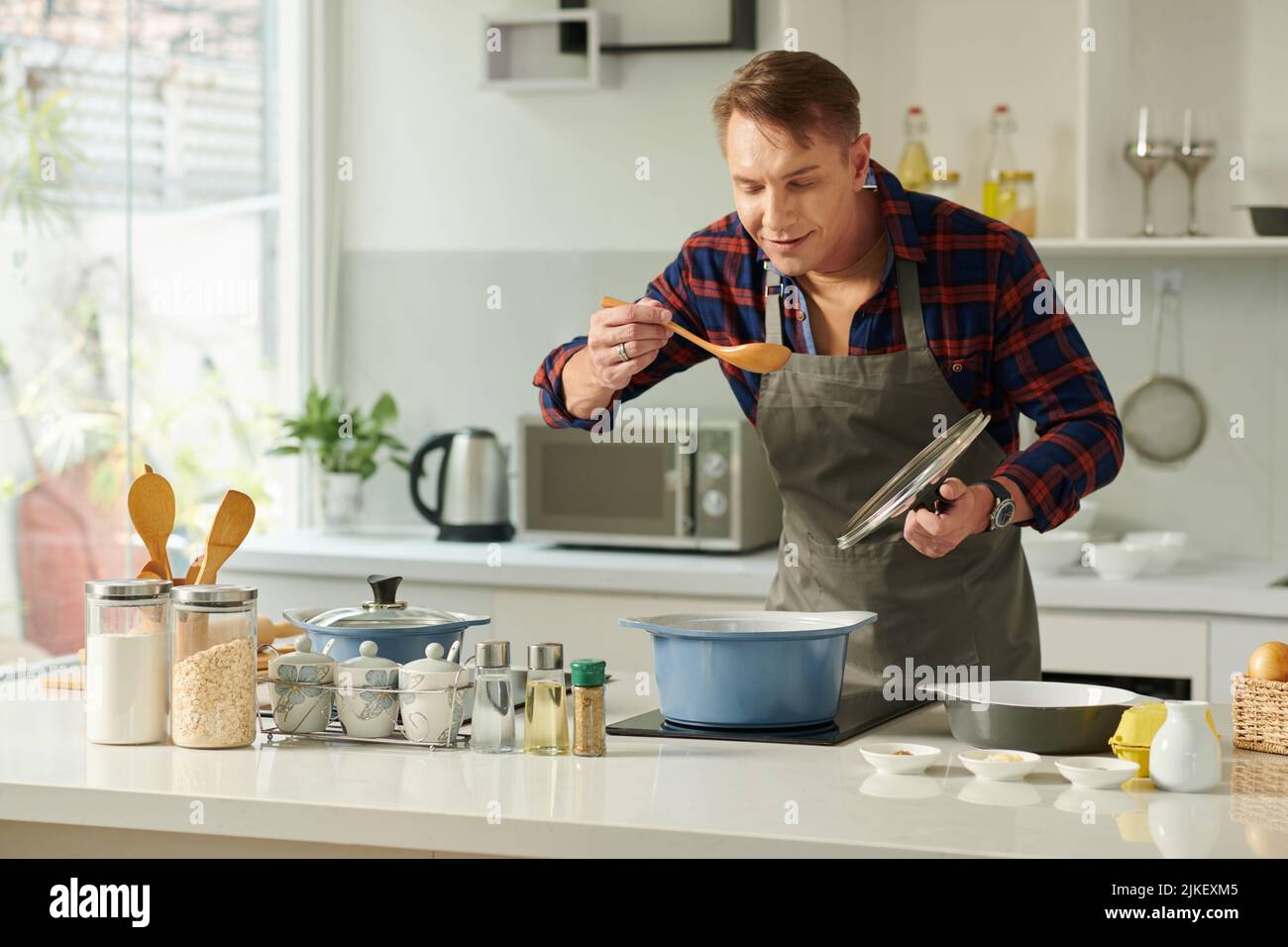 Happy man enjoying smell of delicious soup he is cooking for dinner ...