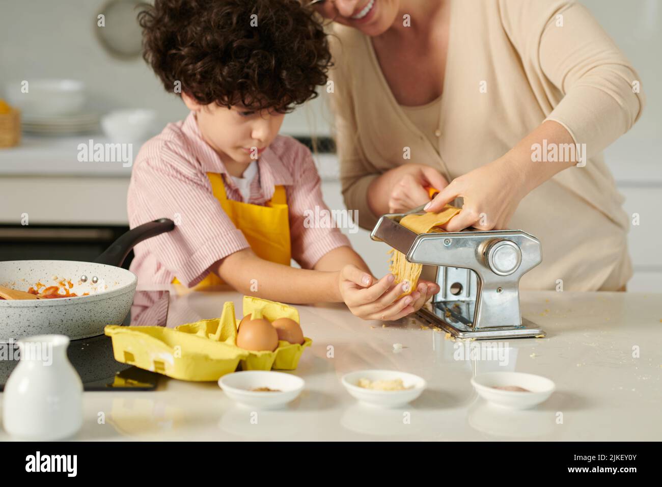 Mother and son using pasta machine to prepare spaghetti for dinner ...
