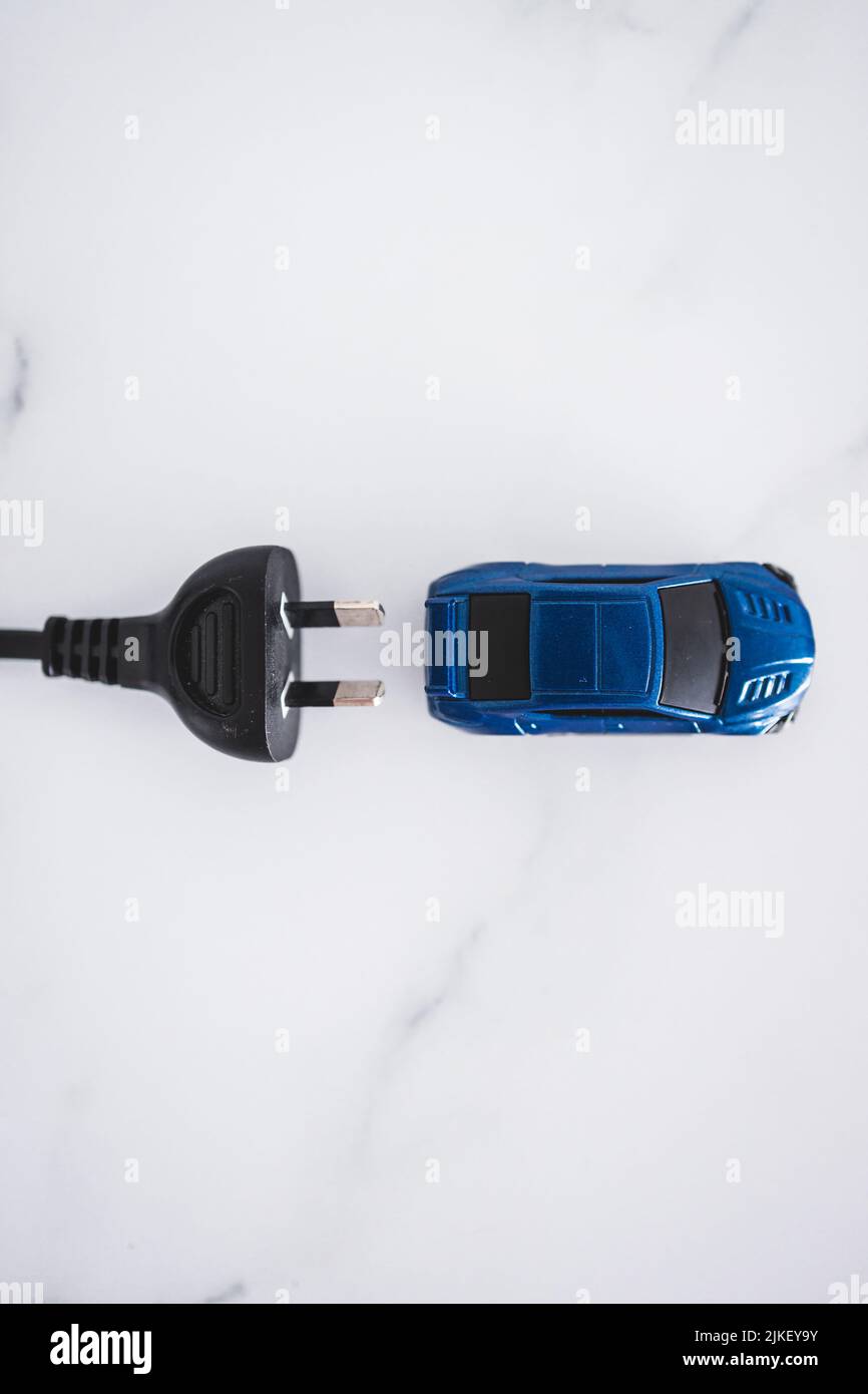 concept of electric or hybrid vehicles, blue toy car with plug behing ...