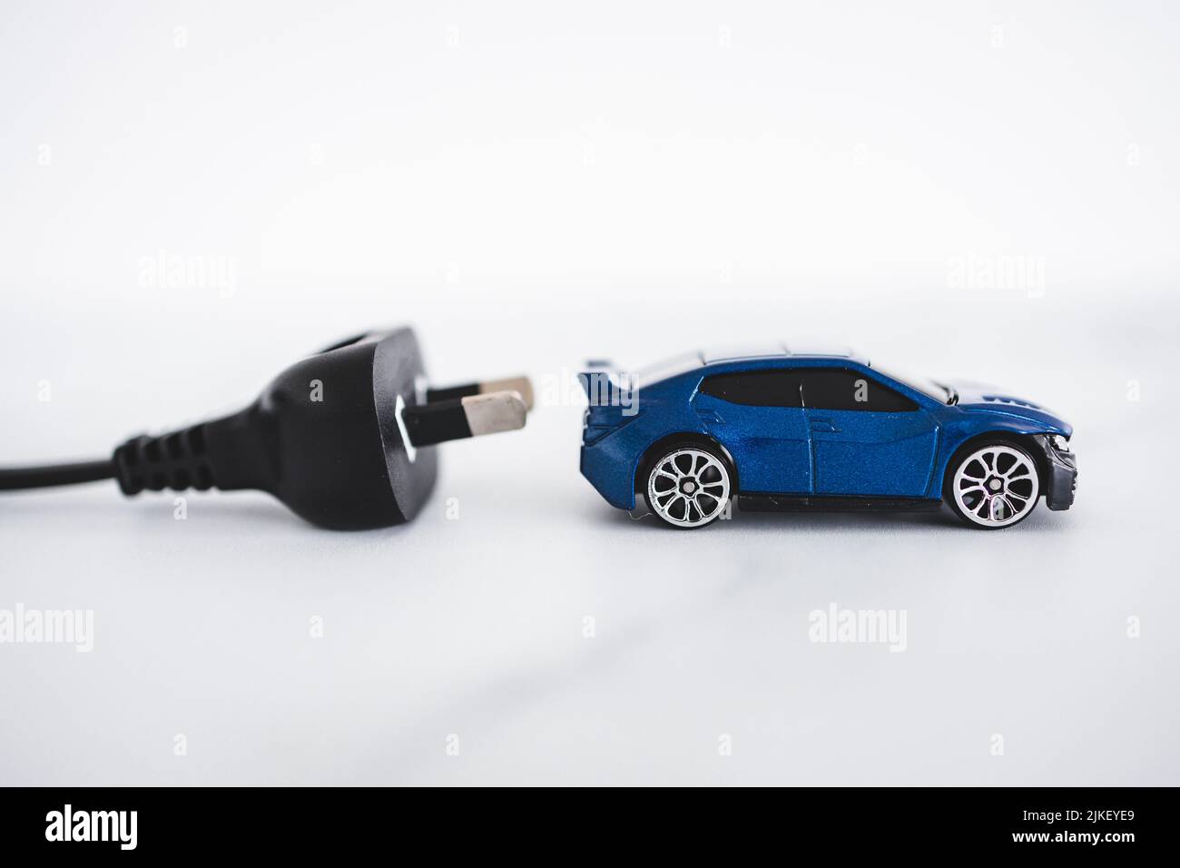 concept of electric or hybrid vehicles, blue toy car with plug behing ...