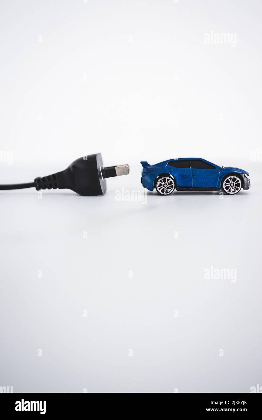 concept of electric or hybrid vehicles, blue toy car with plug behing ...