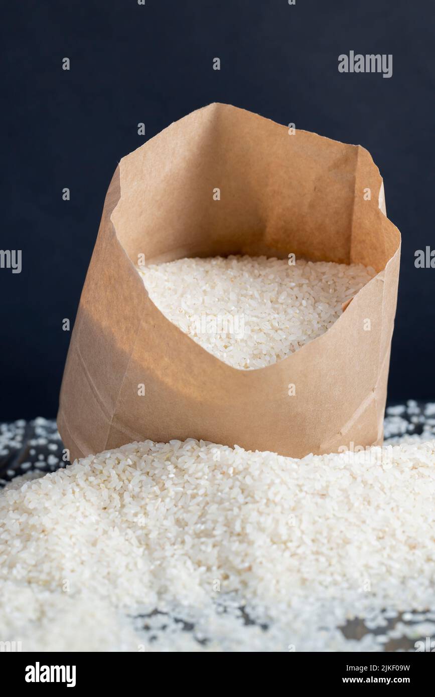 a pile of white rice in a paper bag and on the table, white uncooked ...