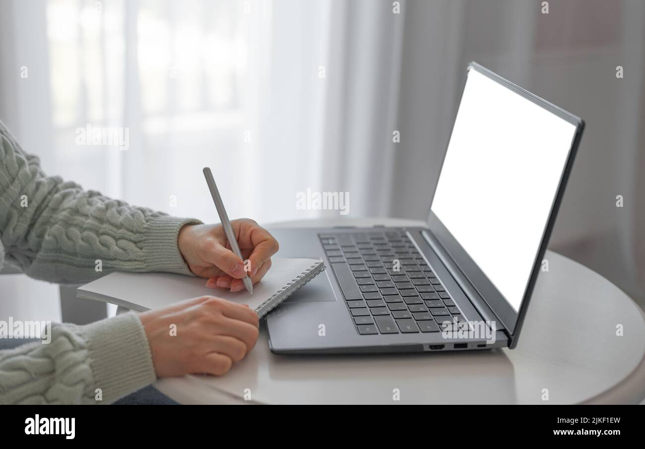 woman taking notes in notebook while using mockup laptop with blank ...