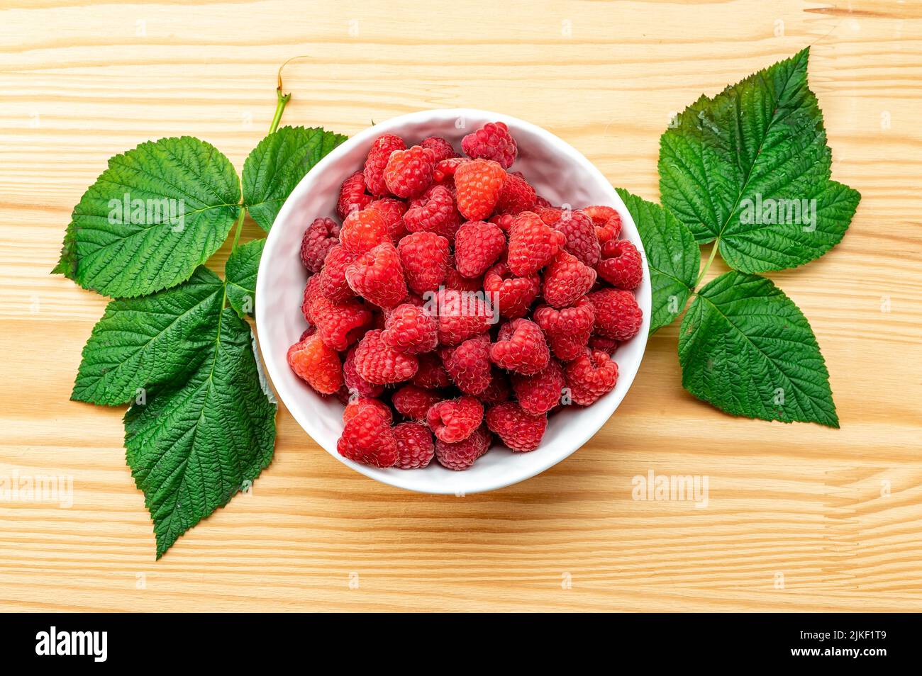 Raspberries on white plate on wooden table with leaves. Organic ...