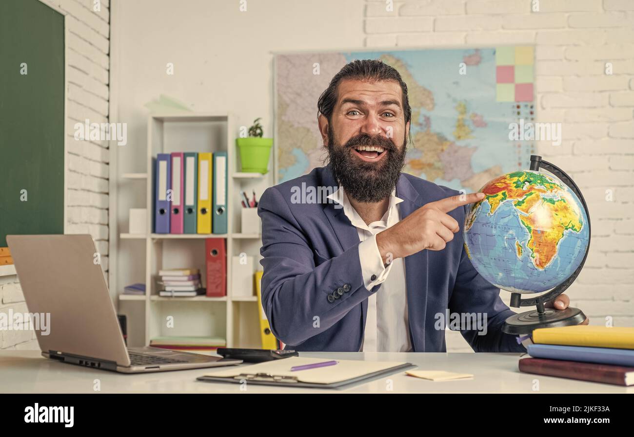 Male teacher in the classroom teaching geography pointing to a world ...