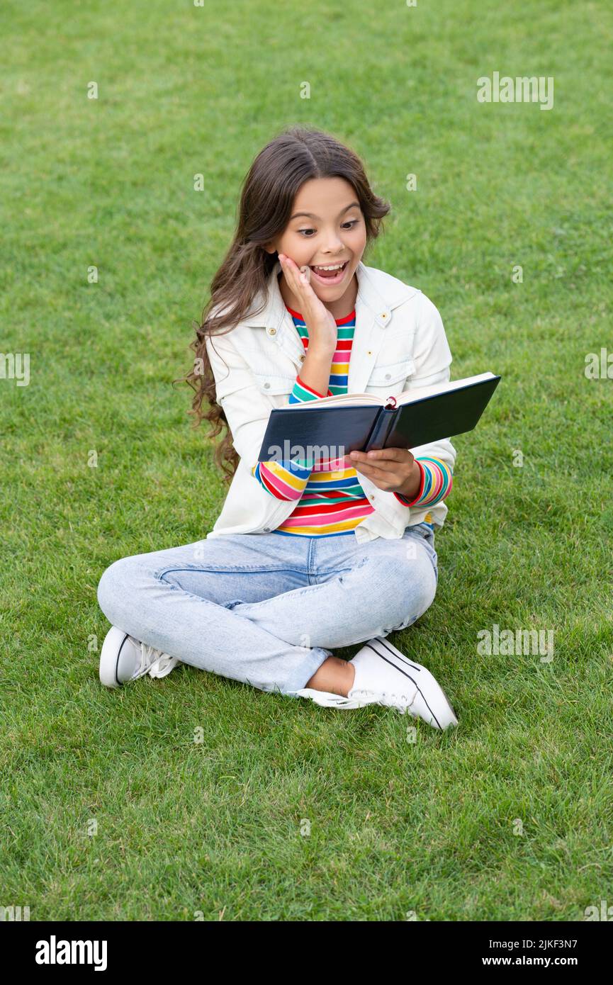 surprised teen girl read book sitting on grass. reading book. reader ...