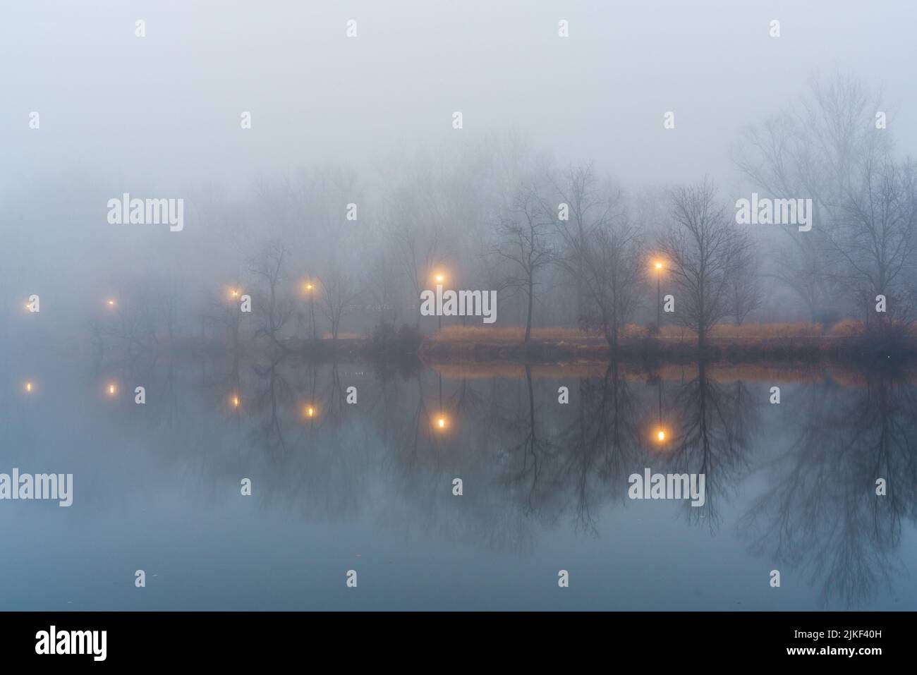 A heavy fog over the water with the reflection of trees and street ...